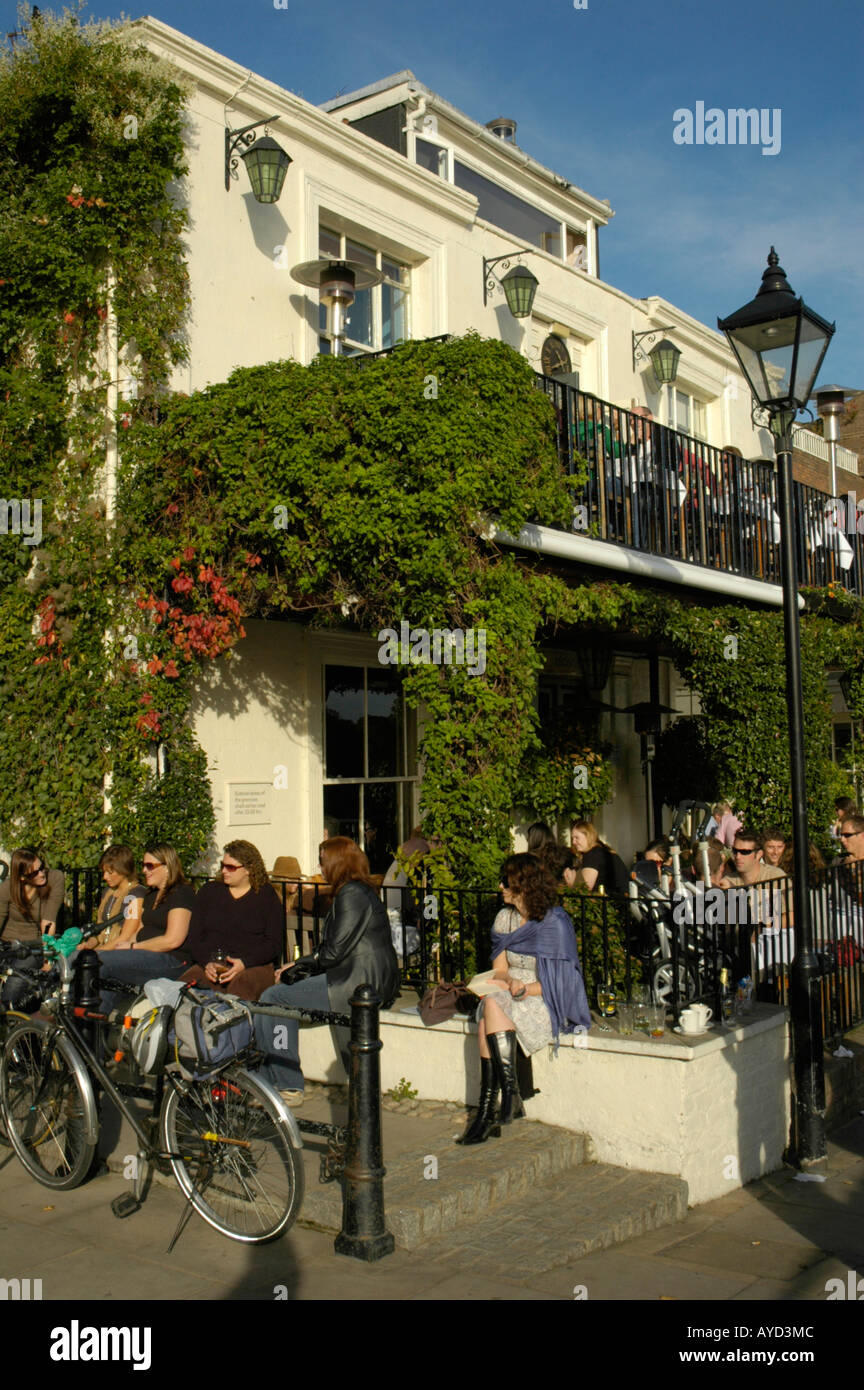 People enjoying the sun outside ivy covered riverside pub next to the ...
