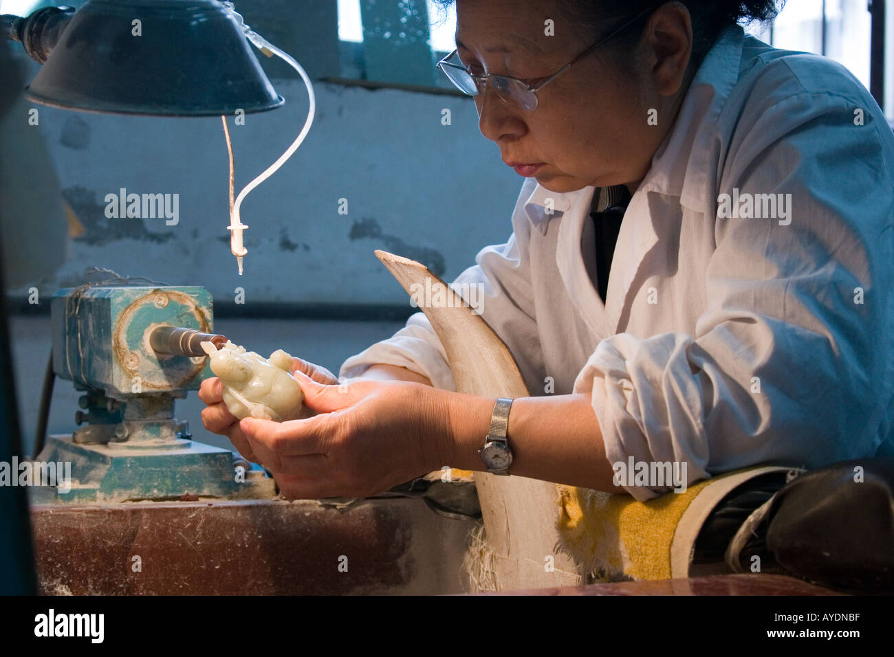 Chinese craftswoman carving a small jade Bhudda in a jade factory ...