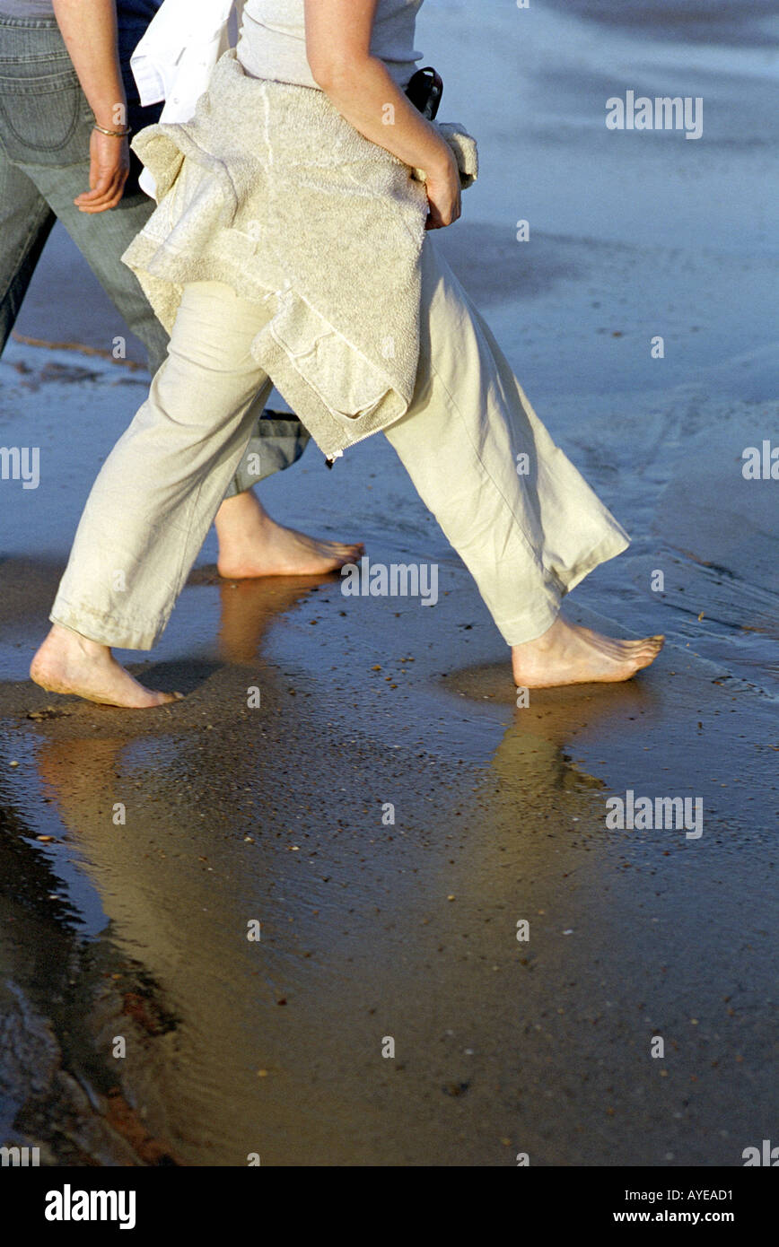 Two women walking barefoot on beach carrying shoes at sunset, faces ...