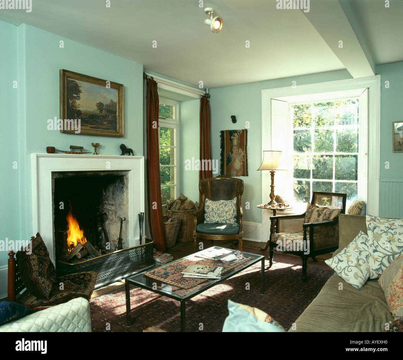 Pale blue traditional country livingroom with fire lit in fireplace ...