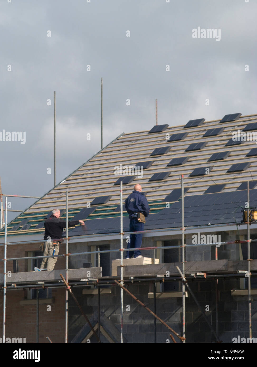 Building house roofers on scaffolding working attaching tiles to wooden ...