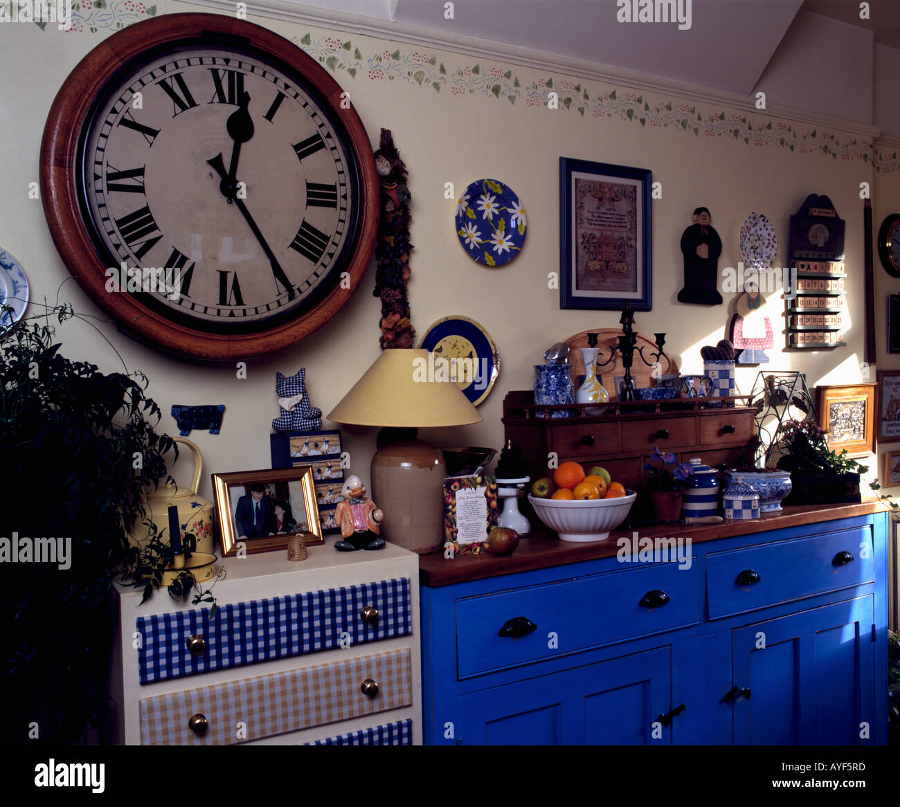 Clock above decorated drawers and blue sideboard in cottage kitchen ...