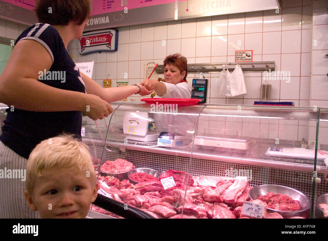 Mother purchasing meat in butcher shop while upset boy tries to escape ...