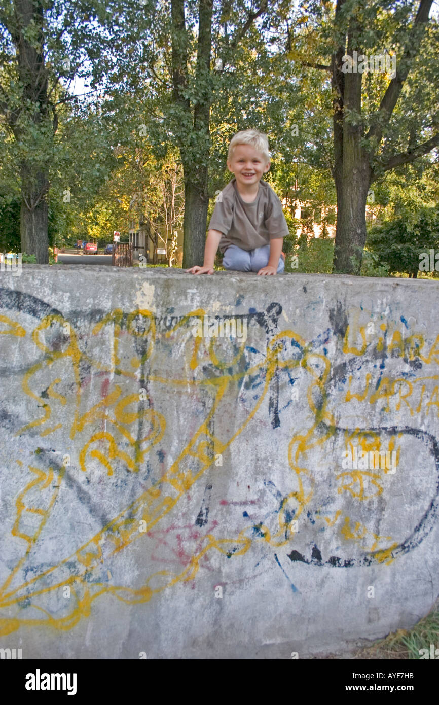 Boy age three having fun climbing on graffiti marked retaining wall ...