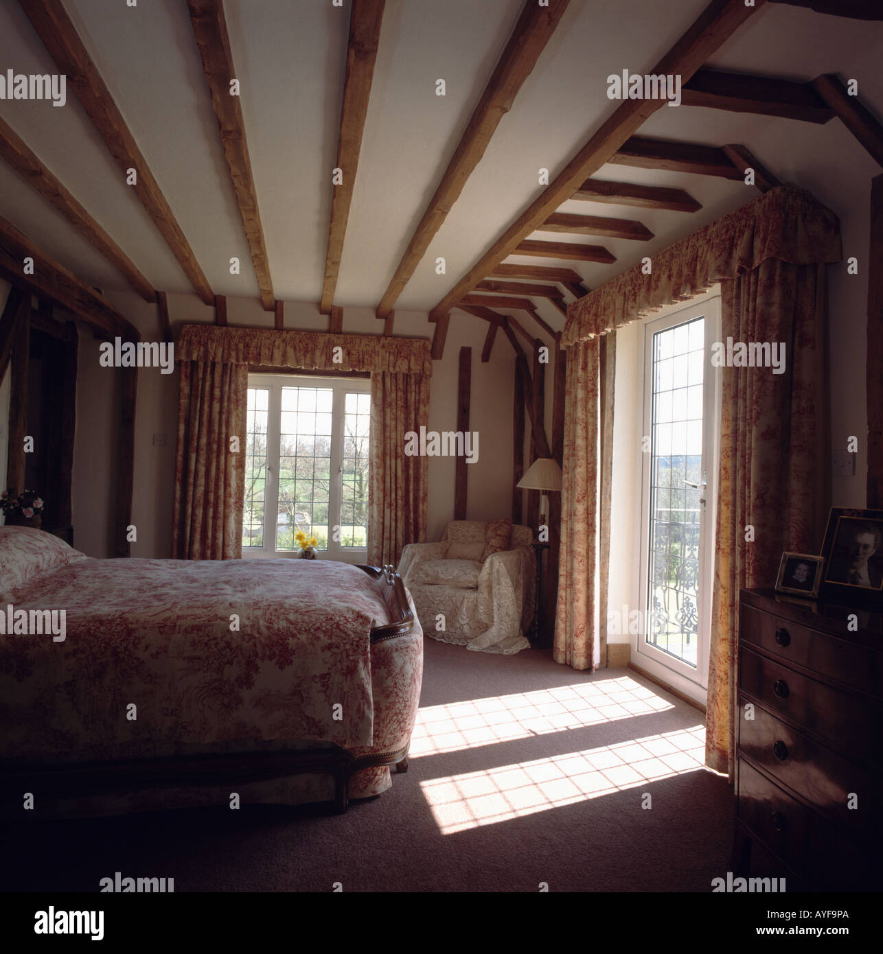 Country bedroom with beamed walls and view of garden through windows ...