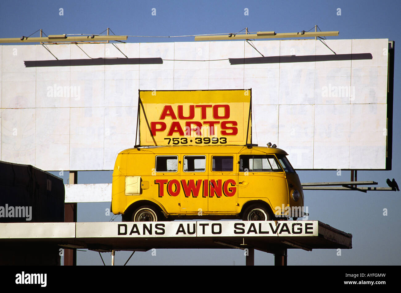 A volkswagen mini bus is displayed on the roof of an auto salvage yard ...