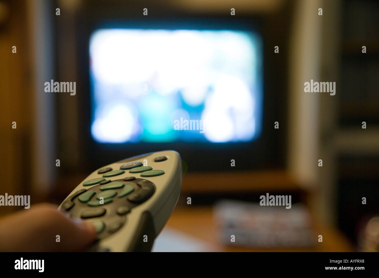 Man's left hand operating Sky remote control with television set in the ...
