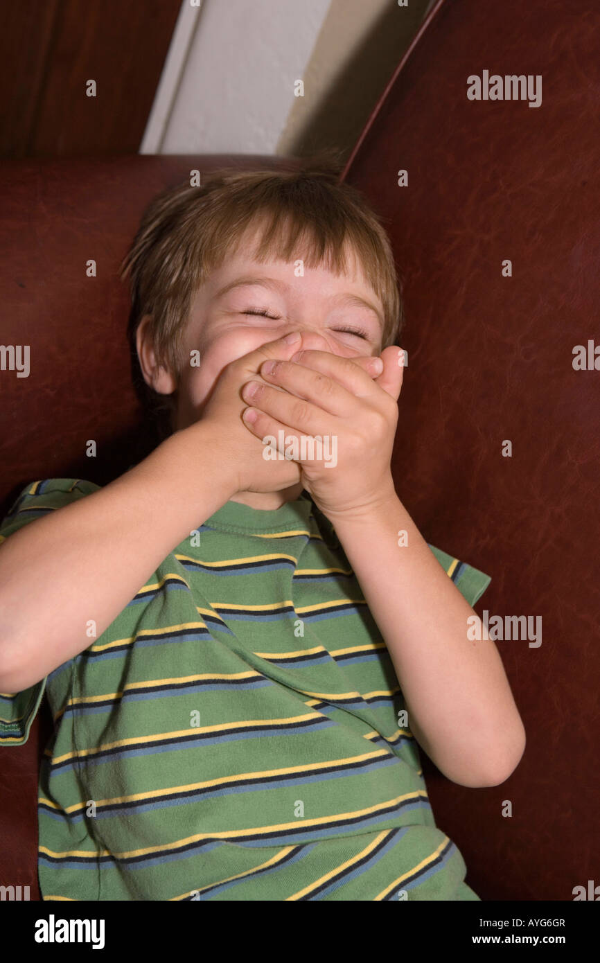 five year old boy covering mouth with both hands, trying not to laugh ...