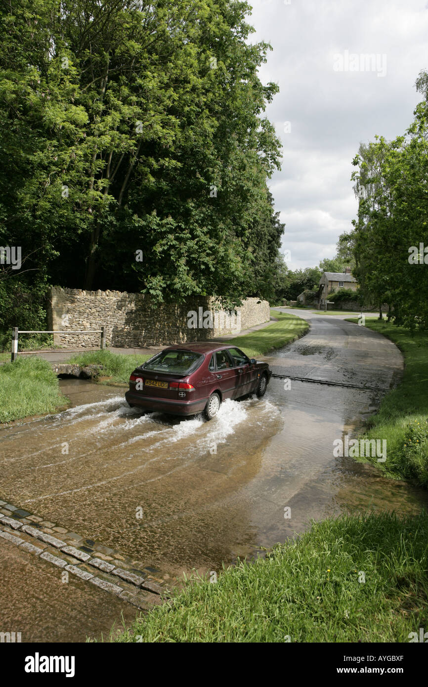 A Saab car going though a shallow ford in the cotswold village of ...