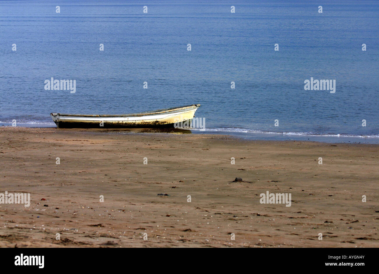 Empty boat on an empty beach with a blue sea behind it Stock Photo - Alamy