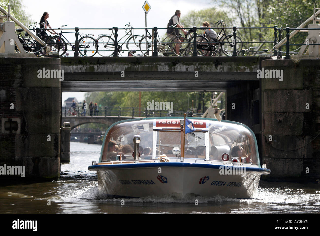 Canal tour boat passes under bridge with cyclists overhead Amsterdam ...