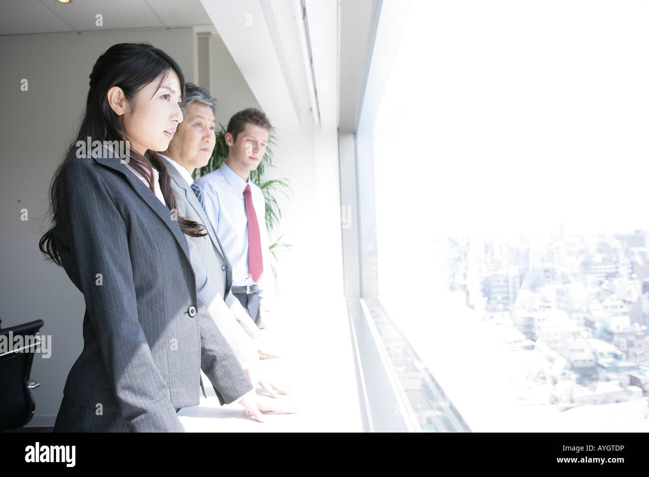 Three business people standing by window looking view Stock Photo - Alamy