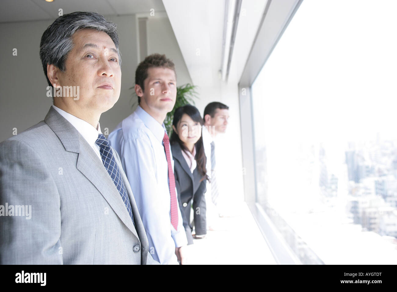 Three business people standing by window looking view Stock Photo - Alamy