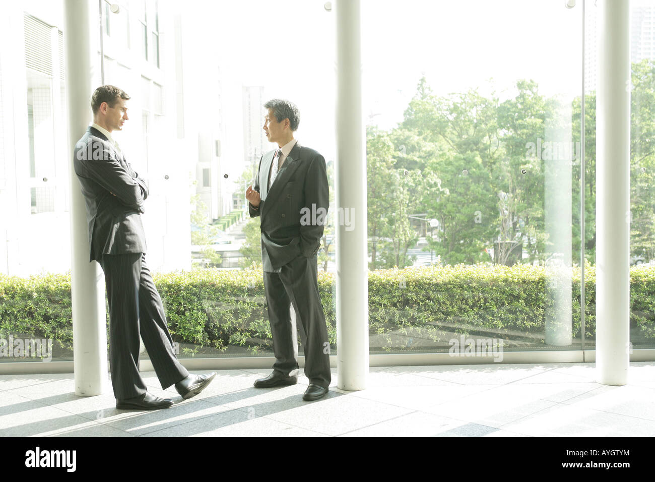 Two businessmen talking in office building lobby Stock Photo - Alamy