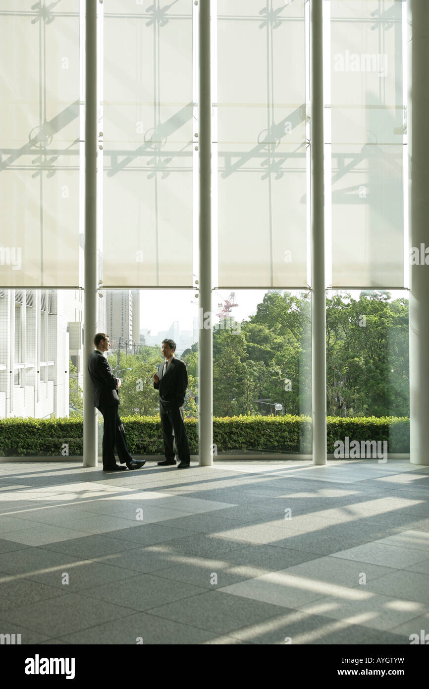Two businessmen talking in office building's lobby Stock Photo - Alamy