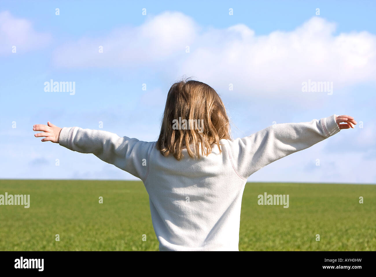 Shot of a young girl with her arms stretched out looking over a green ...