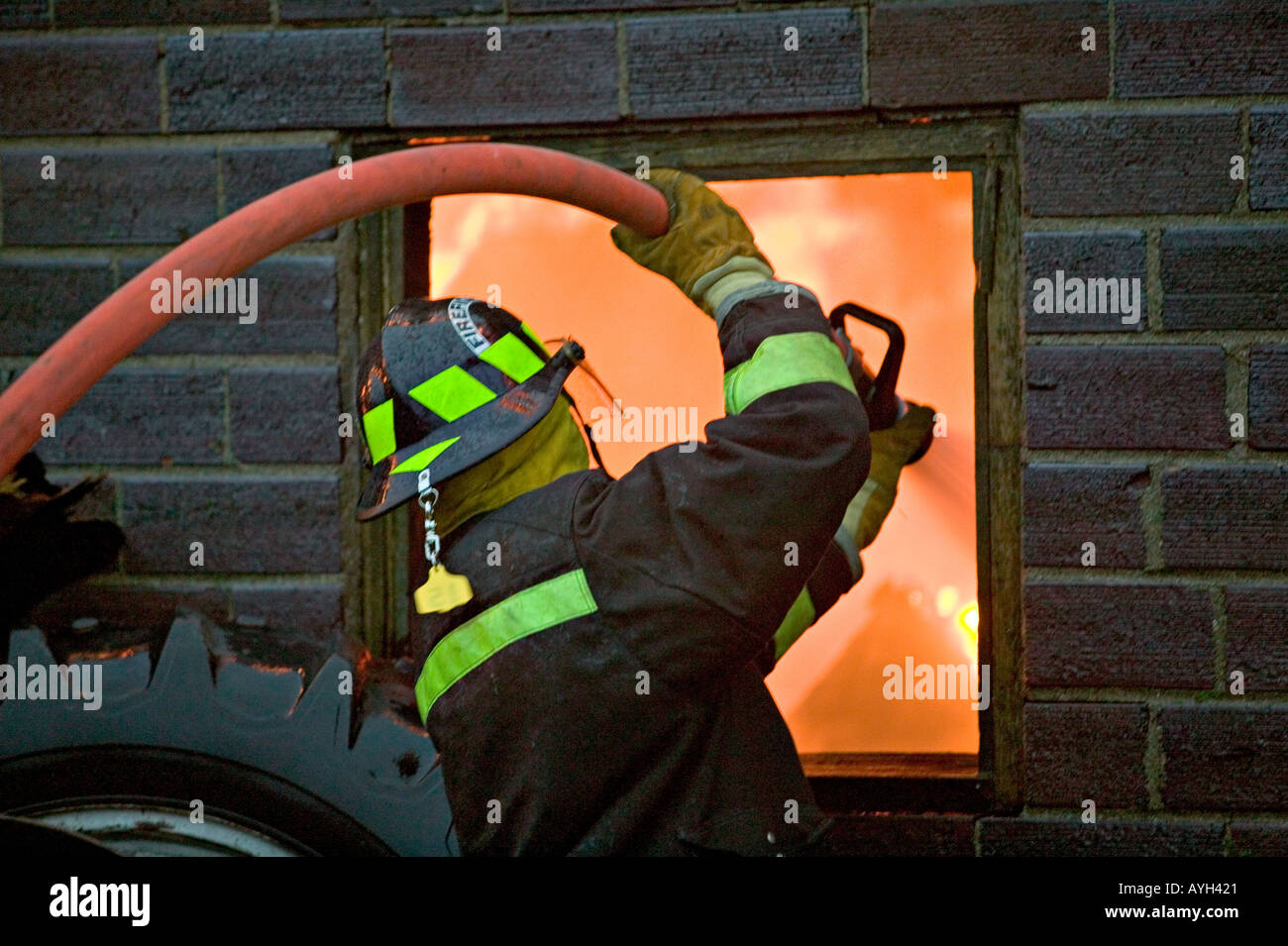 Firefighter applying water through window of burning building Stock ...