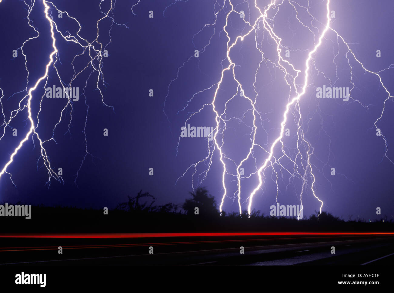 Lightning bolts strike in during a desert monsoon with car tail lights ...