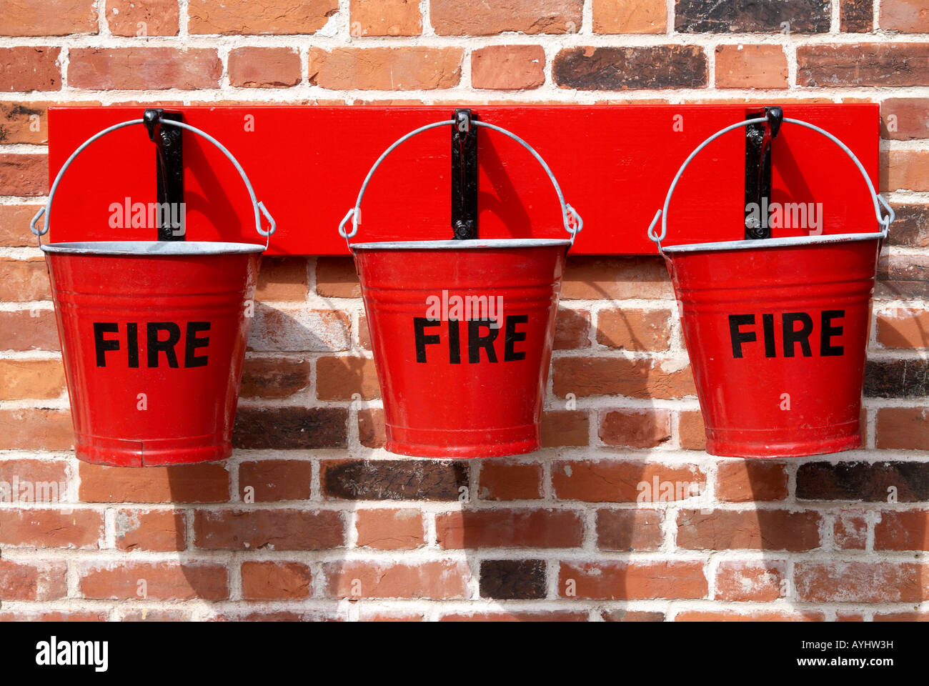 Red fire buckets hanging from red back board against a brick wall Stock ...