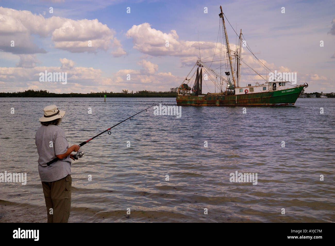 Angler fishing while shrimp boat passes Stock Photo - Alamy