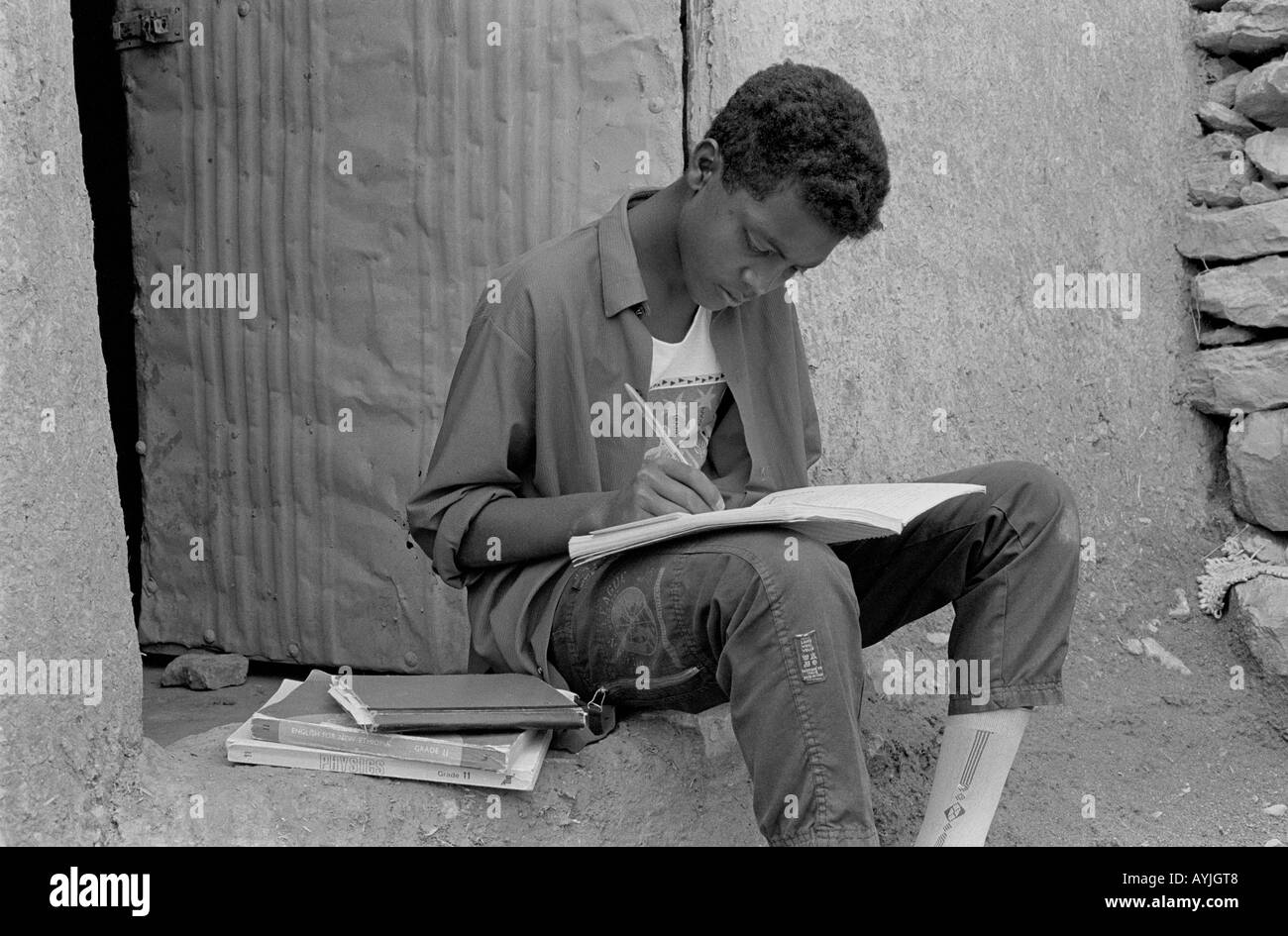 B/W of a poor boy studying with books on the doorstep. Mekelle, Tigray ...