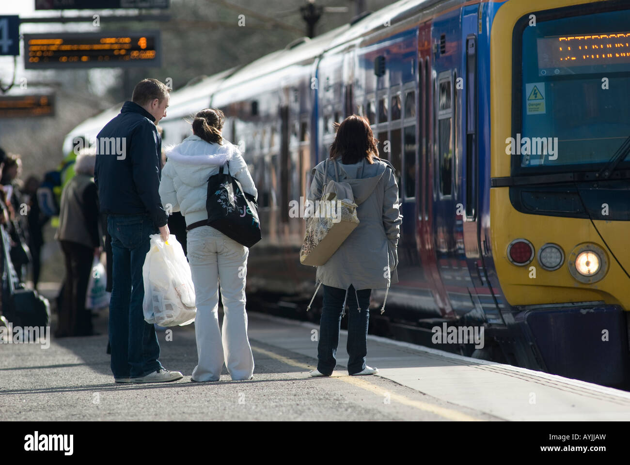 passengers waiting on a railway station platform as a train pulls in in ...