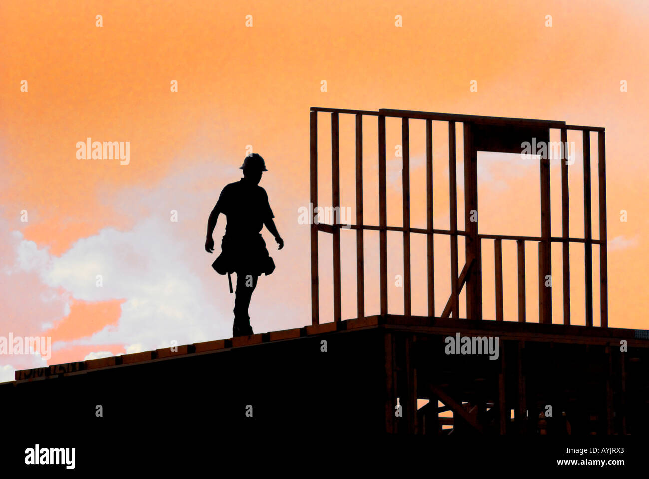 Contruction worker standing on roof of house with orange sky background ...