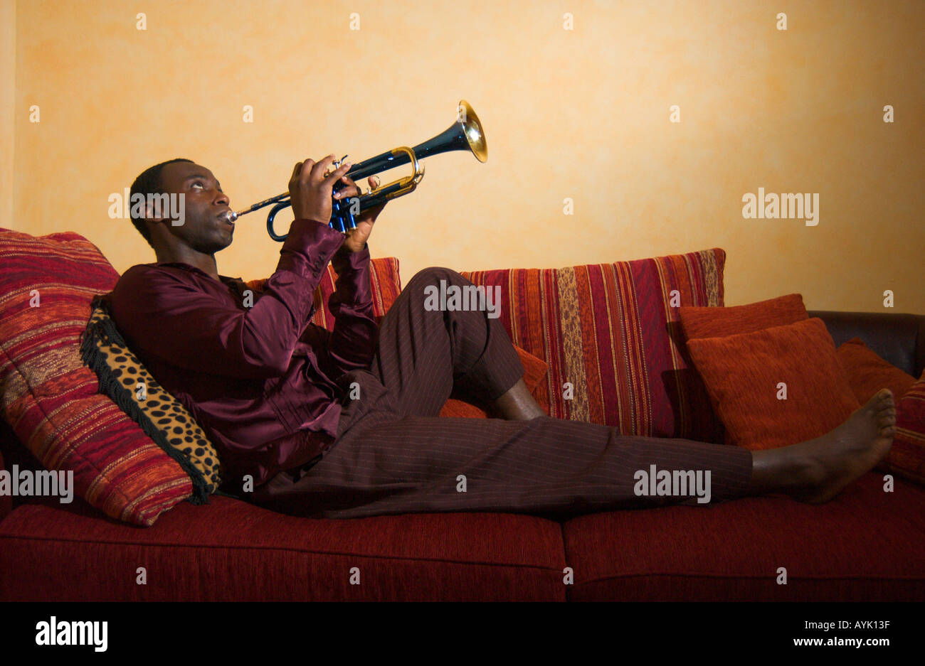 man reclining on red sofa plays blue trumpet Stock Photo - Alamy