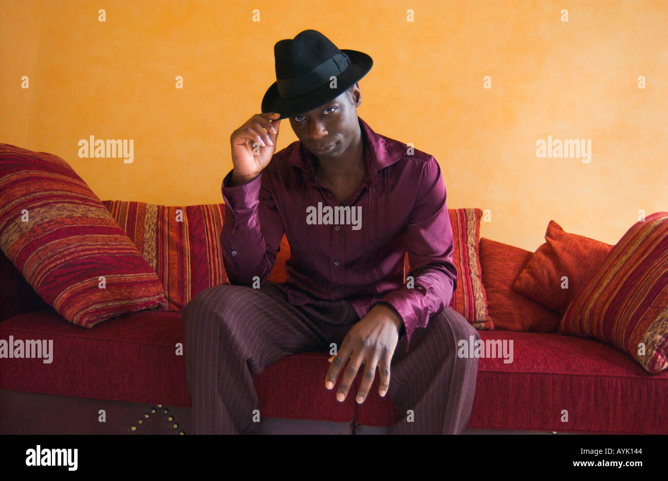 man wearing fedora hat sitting on red couch Stock Photo - Alamy