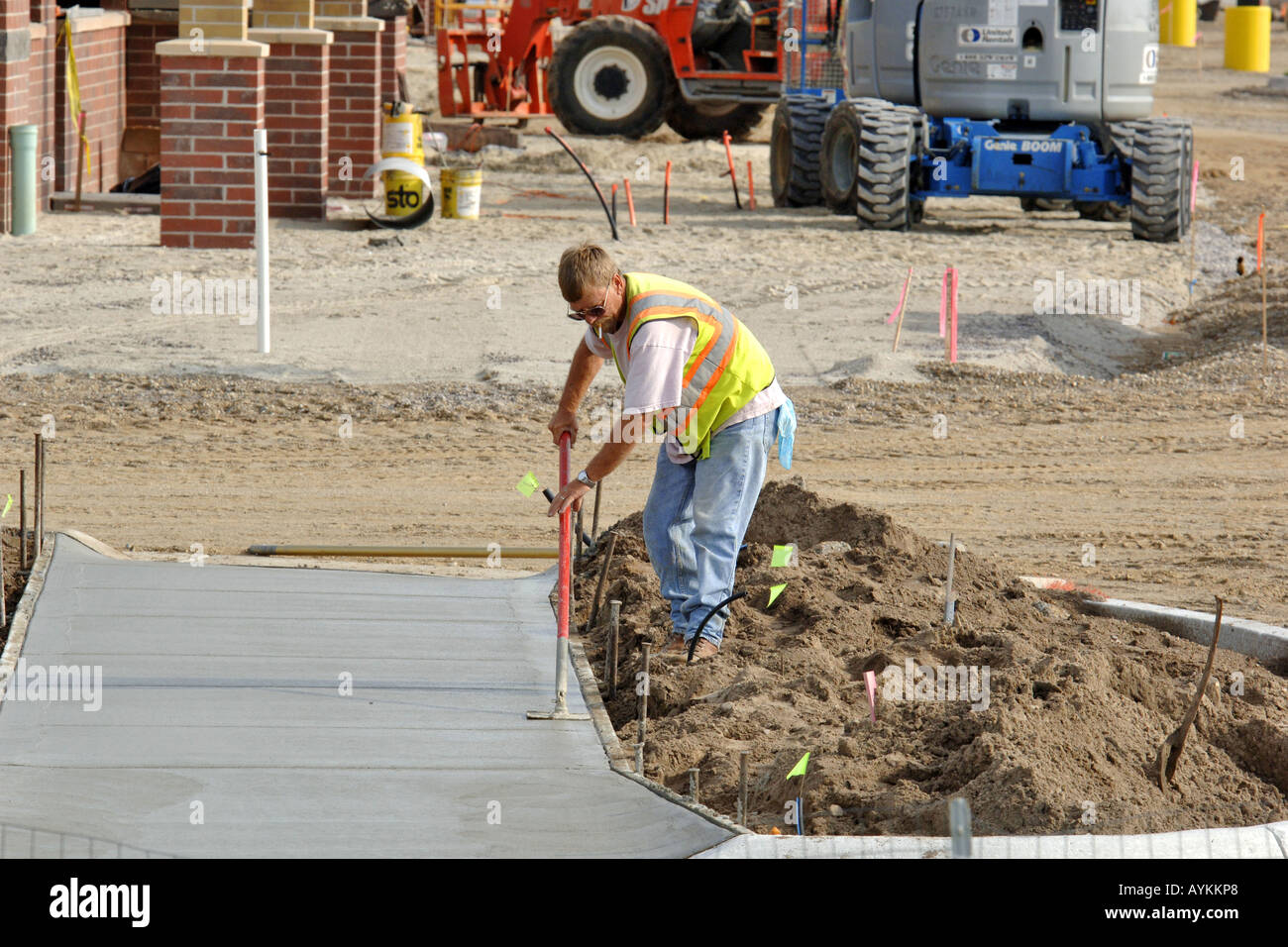 Construction worker leveling a cement path outside a new development in ...