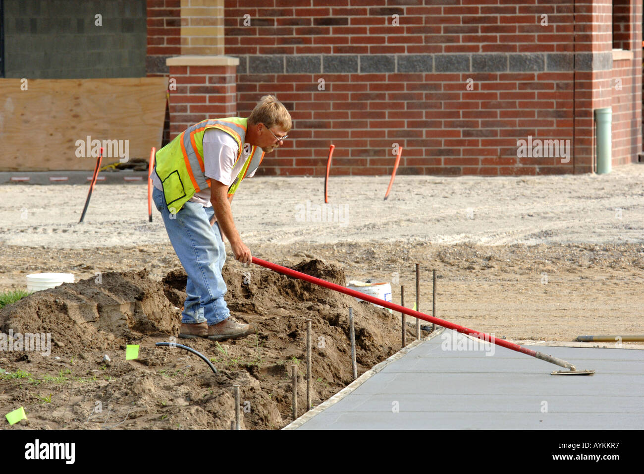 Construction worker leveling a cement path outside a new development in ...