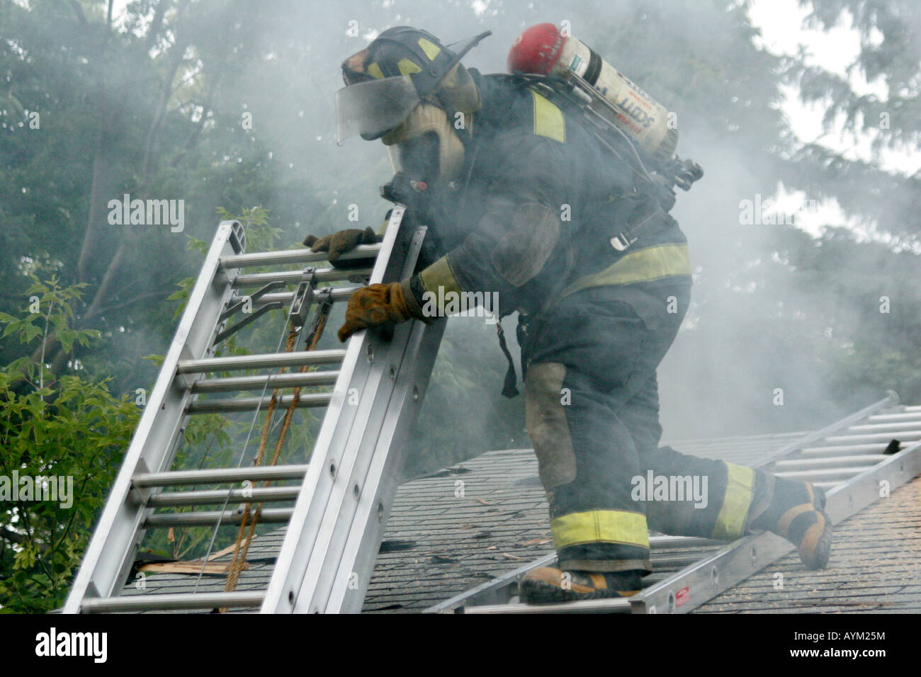 A firefighter climbing down off a roof onto a ladder after cutting ...