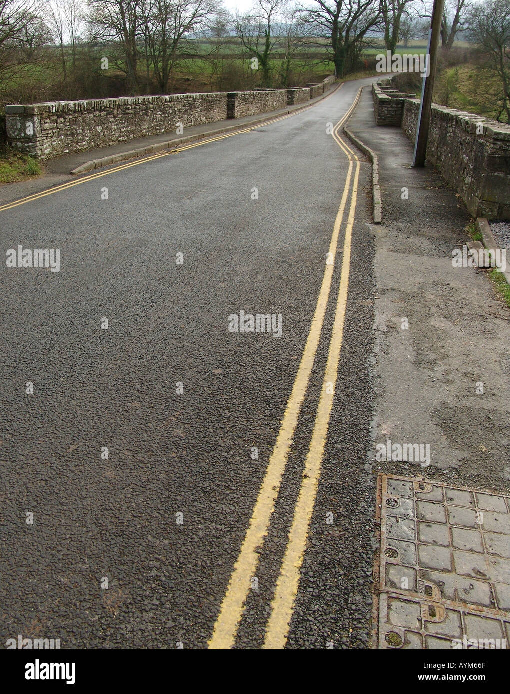A narrow road leading over a bridge with double yellow lines Wales UK ...