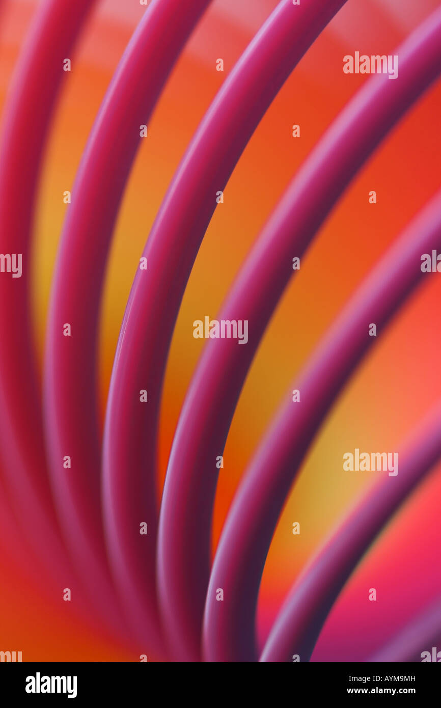 Close up abstract image of a pink Slinky Spring against a yellow orange ...
