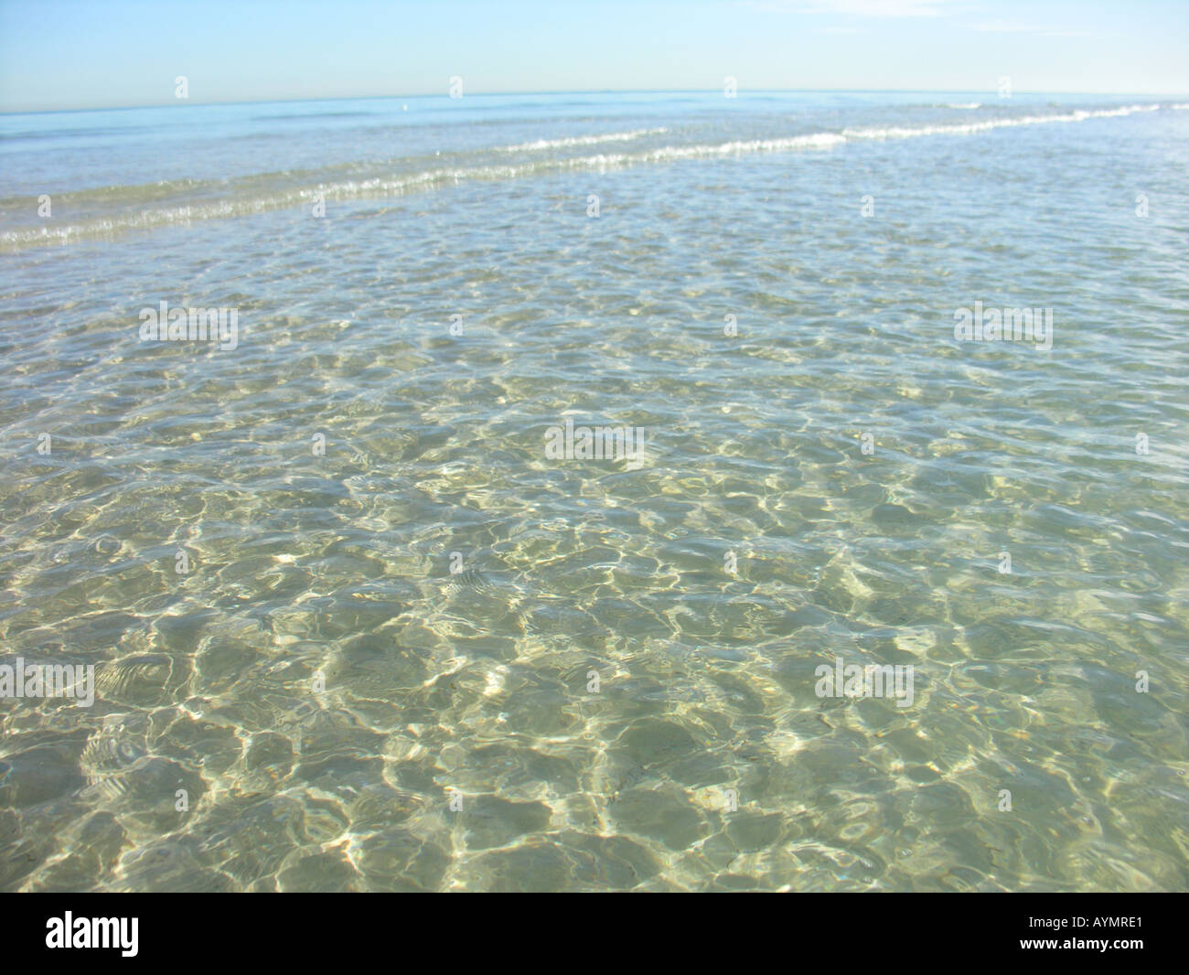 Shallow clear water over sand beach reflecting sun Stock Photo - Alamy