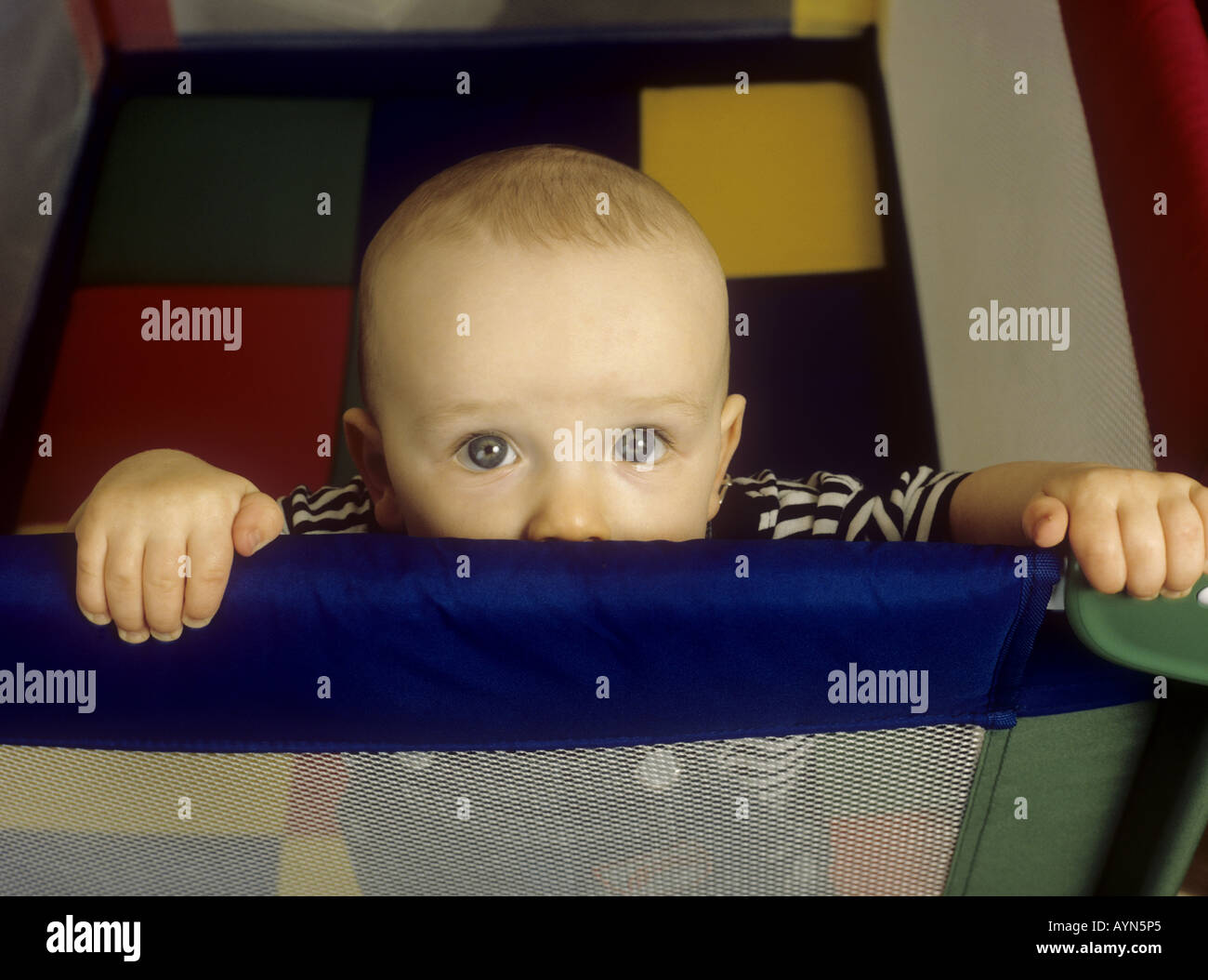 Baby boy peering over the top of a travel cot looking sad Stock Photo ...