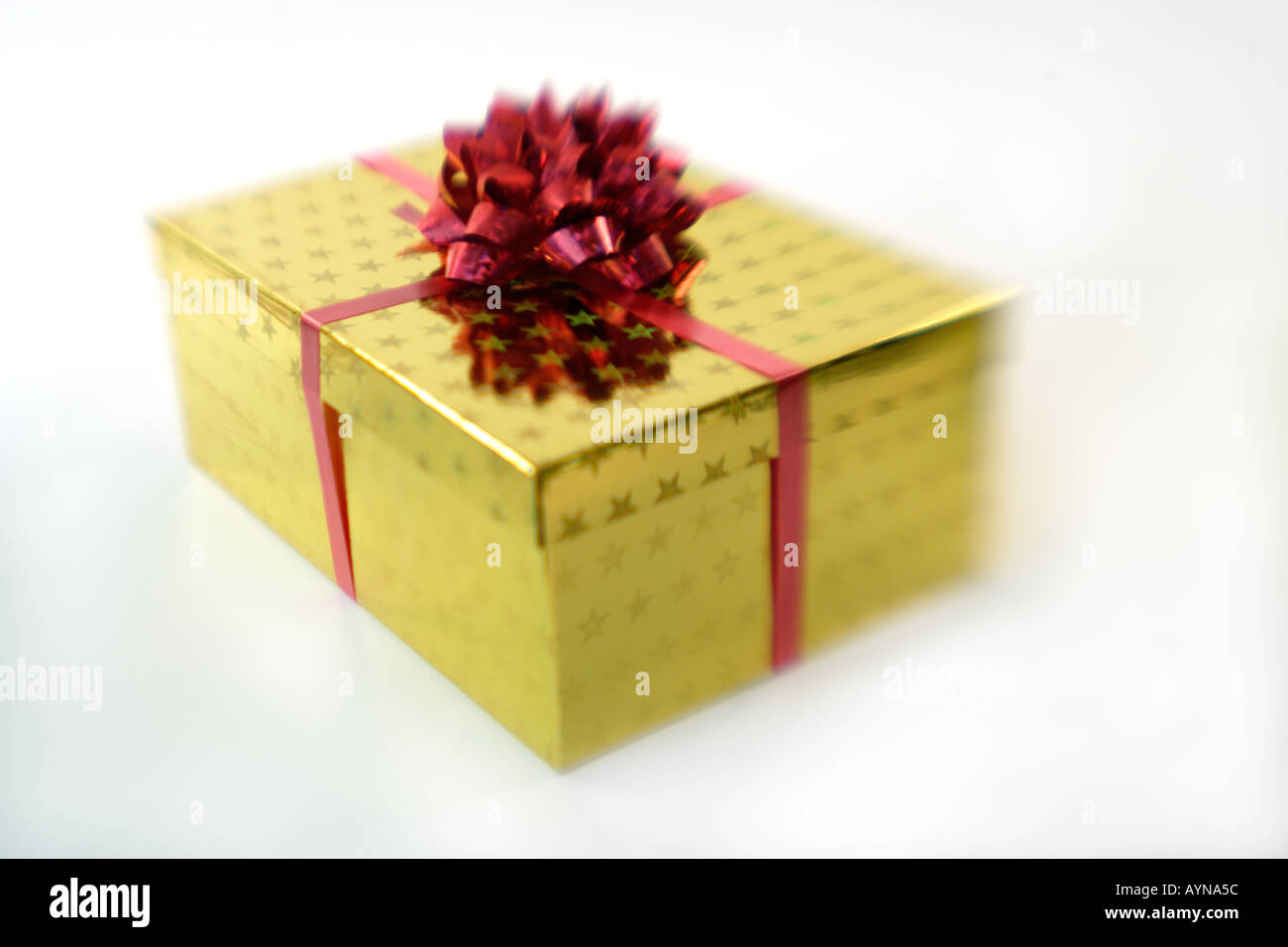 Still life of a shiny gold gift wrapped present with an ornate red bow ...