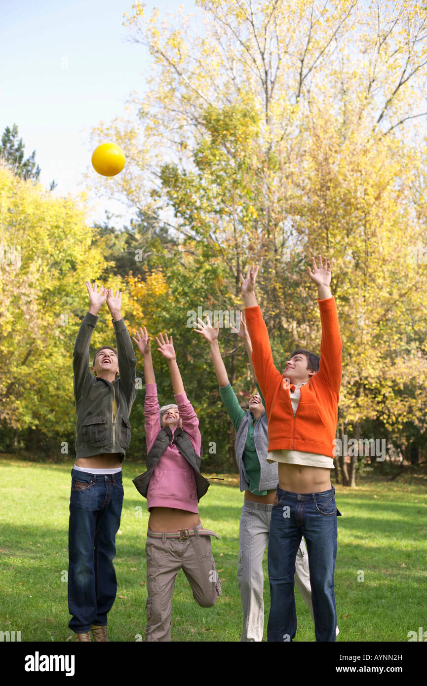 Four teenagers raising their arms to reach a ball in a park Stock Photo ...