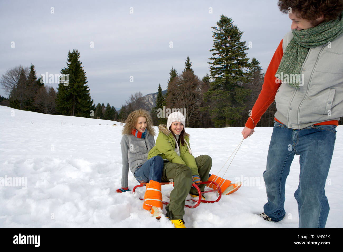 Young man pulling a sled with two women sitting on it Stock Photo - Alamy