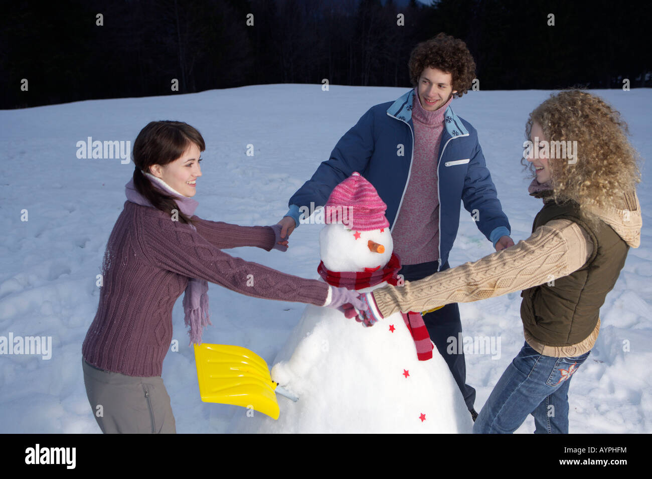 Three young people making a snowman Stock Photo - Alamy