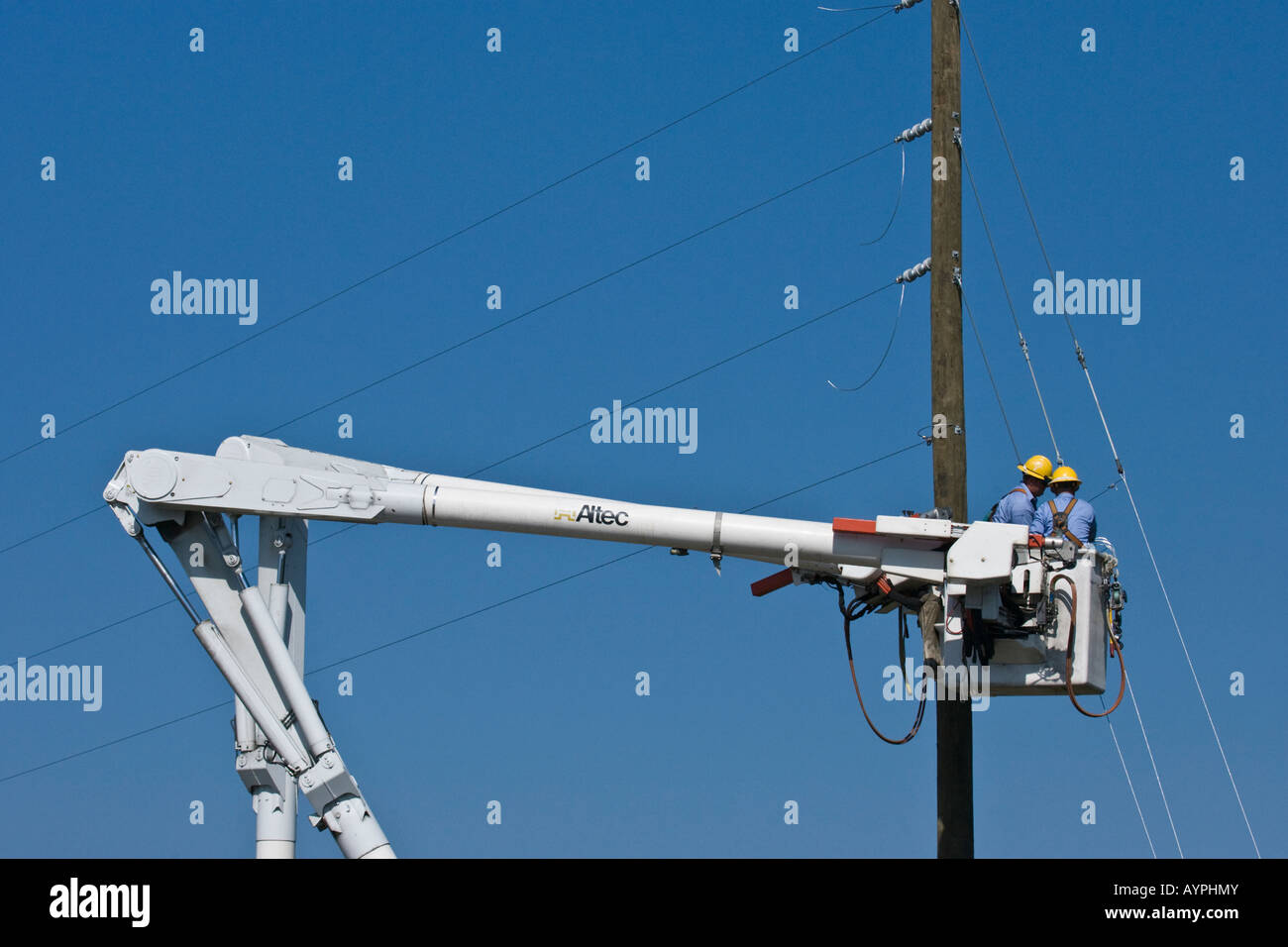 Electrical workers weaving yellow hardhats in a lift working on power ...