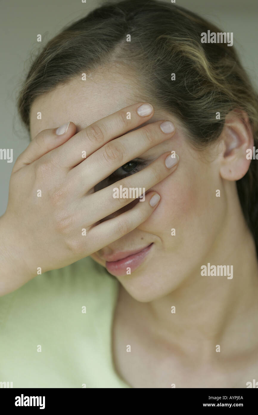 A blonde woman looks through the fingers as she covers her face with ...