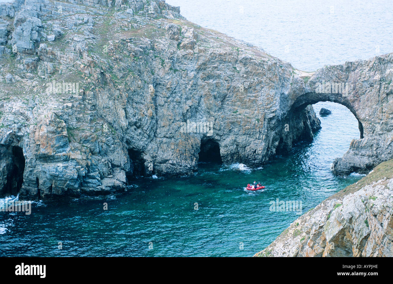 Looking down on people in a red dingy sailing by a natural archway that ...