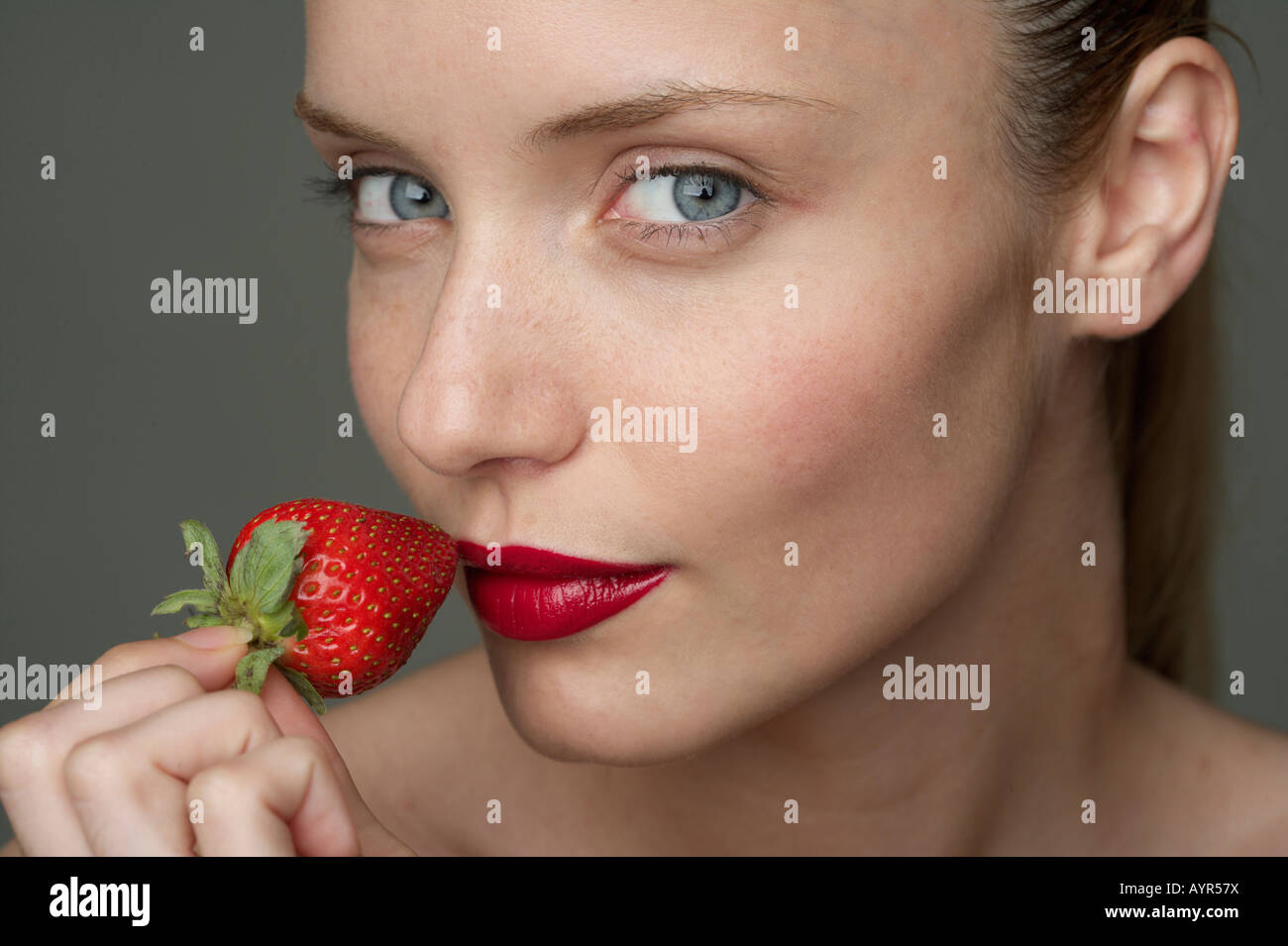 Young woman with a red strawberry under her red lips (part of), close ...