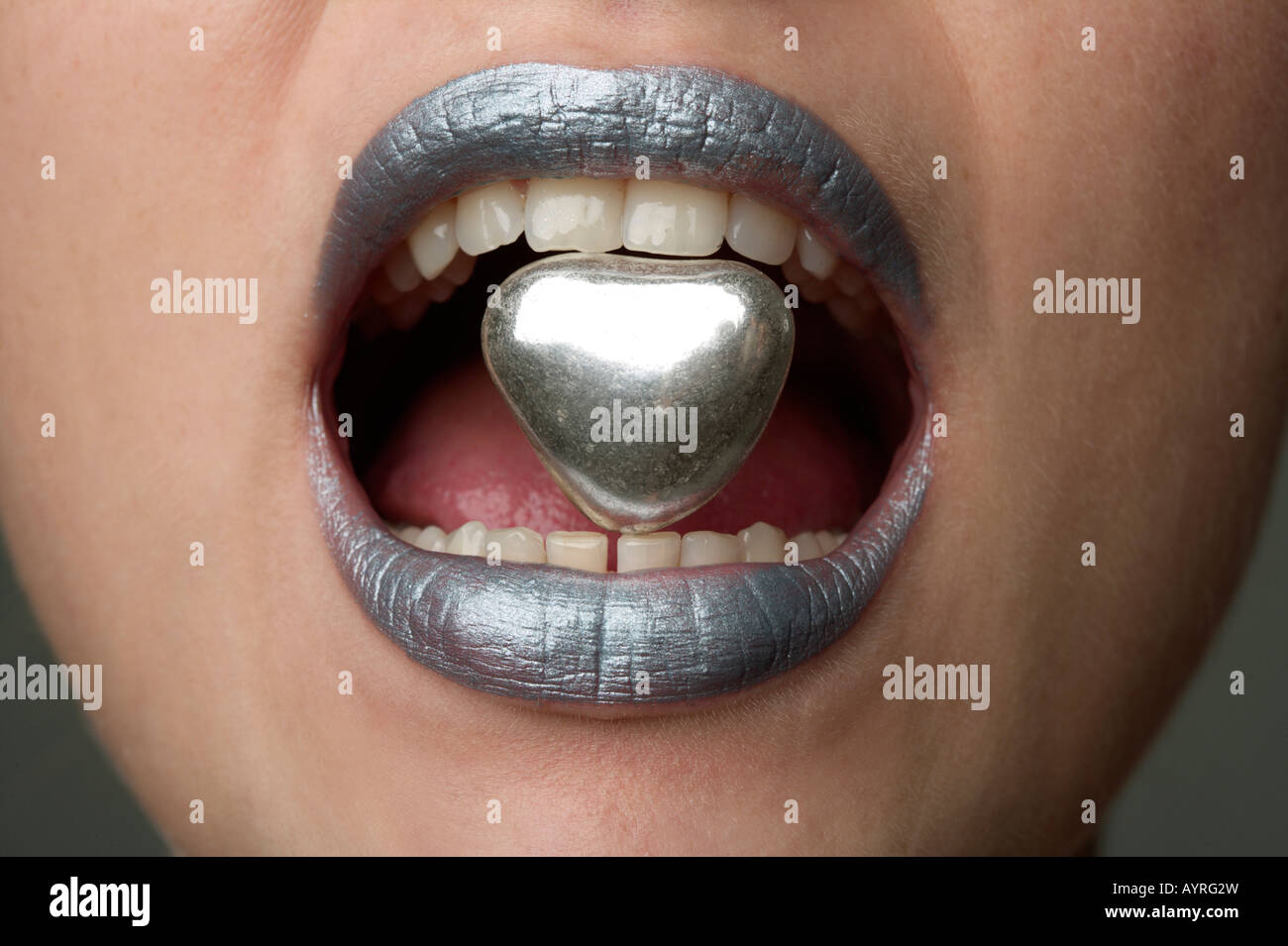 Silver heart between young woman's teeth Stock Photo - Alamy