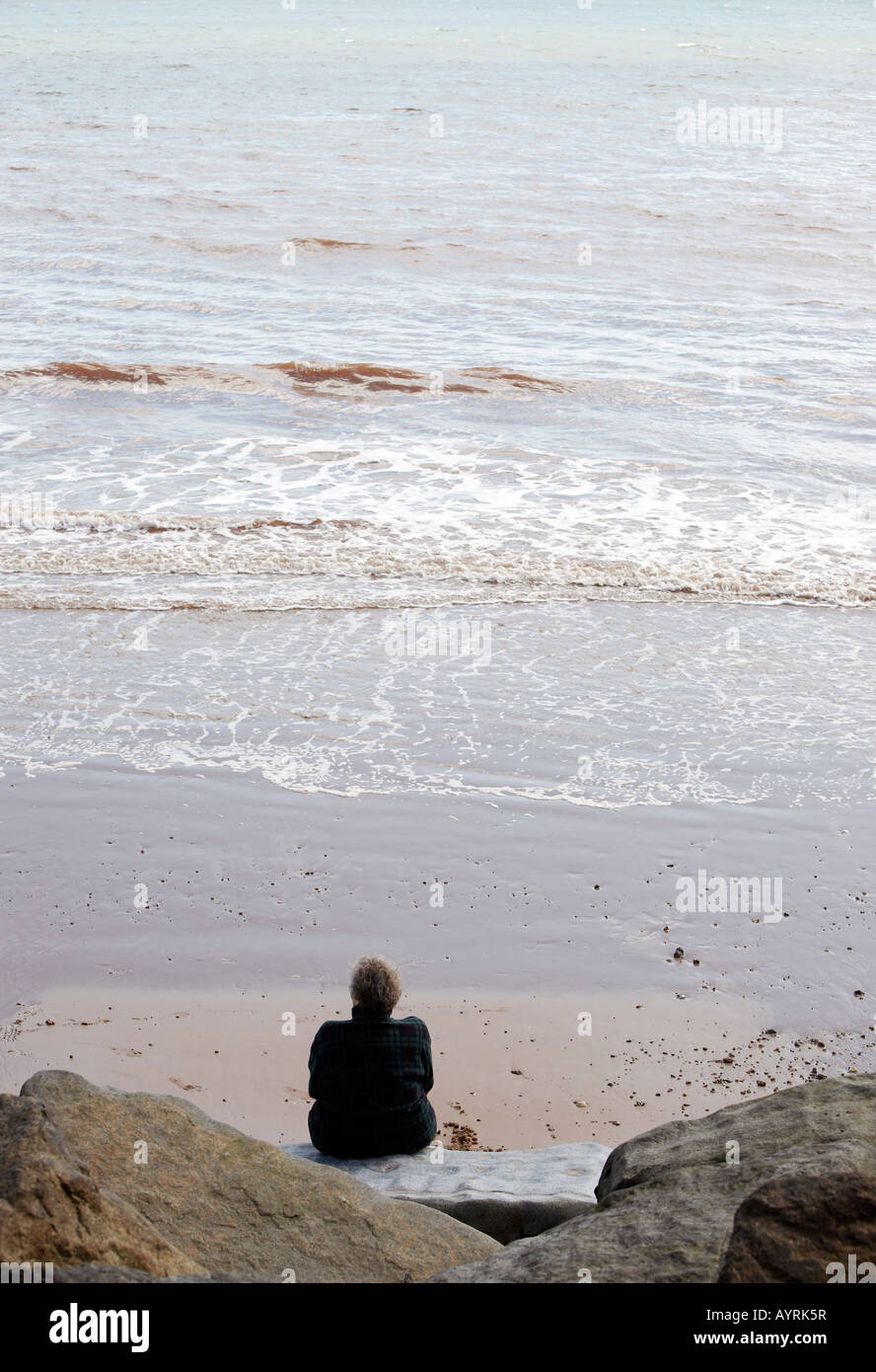 An elderly person sitting on a rock, staring at the sea Stock Photo - Alamy