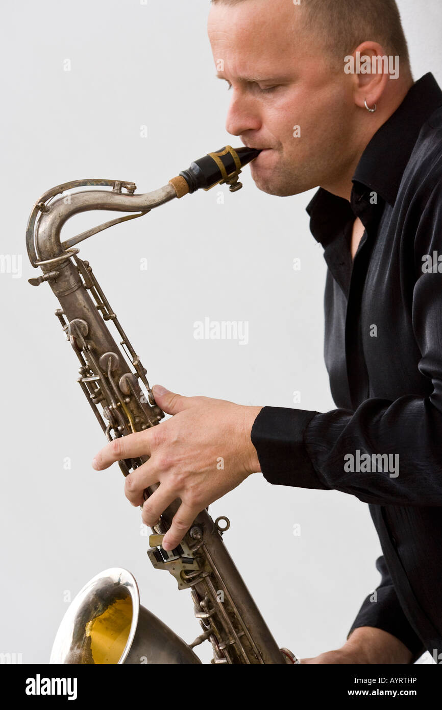 A street musician leaning against a white wall and playing his ...