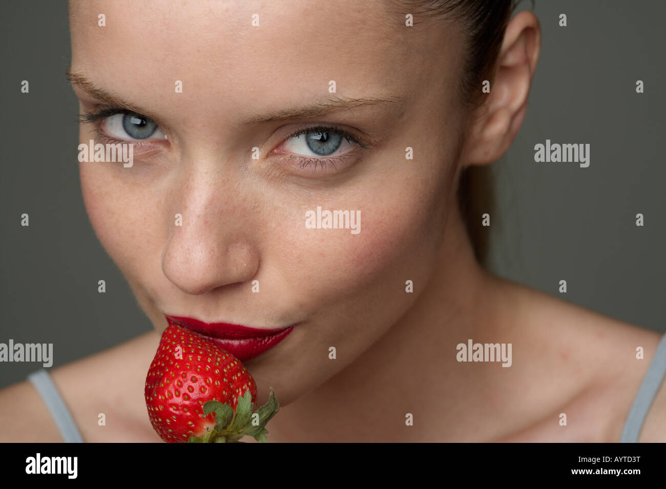 Young woman with a red strawberry under her red lips (part of), close ...