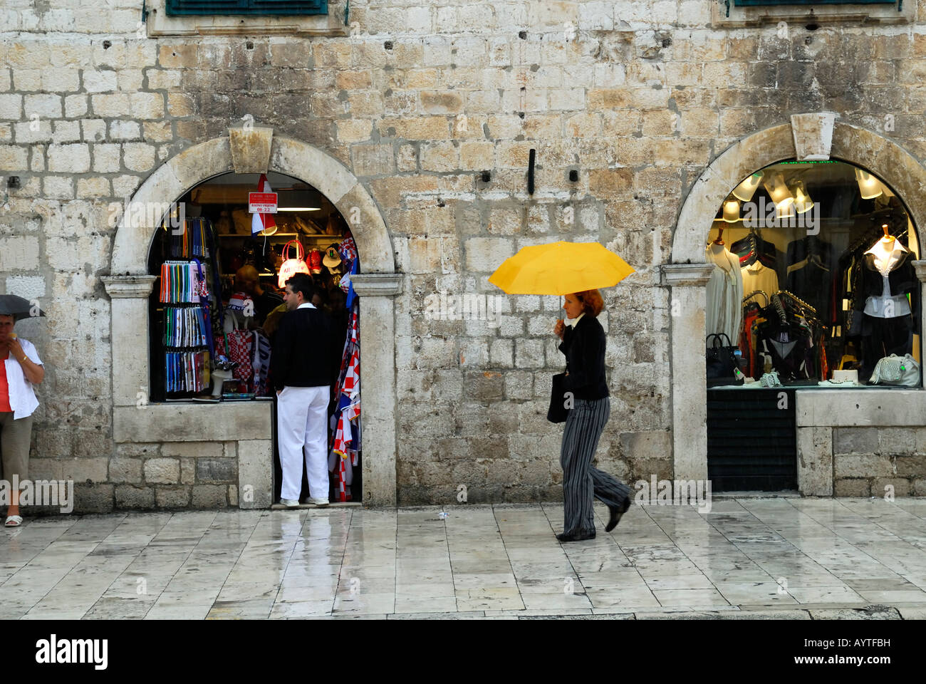 Woman with yellow umbrella walking past "na koljeno" style of door ...