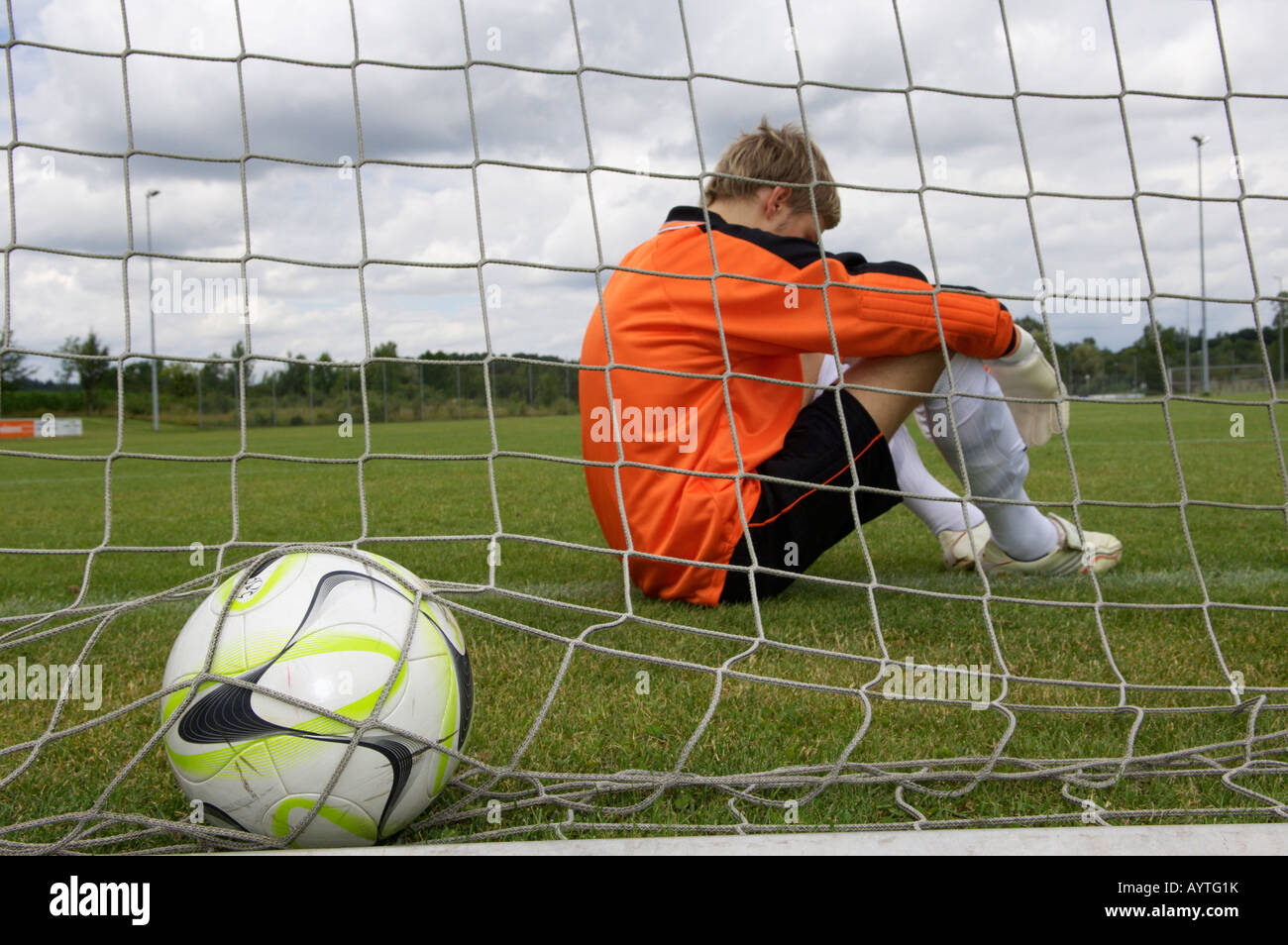 Disappointed goalkeeper sitting in goal, ball in net Stock Photo - Alamy